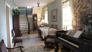 Uma sala de estar espaçosa com um piano de cauda, uma mesa de jantar e uma escadaria que leva a um andar superior.