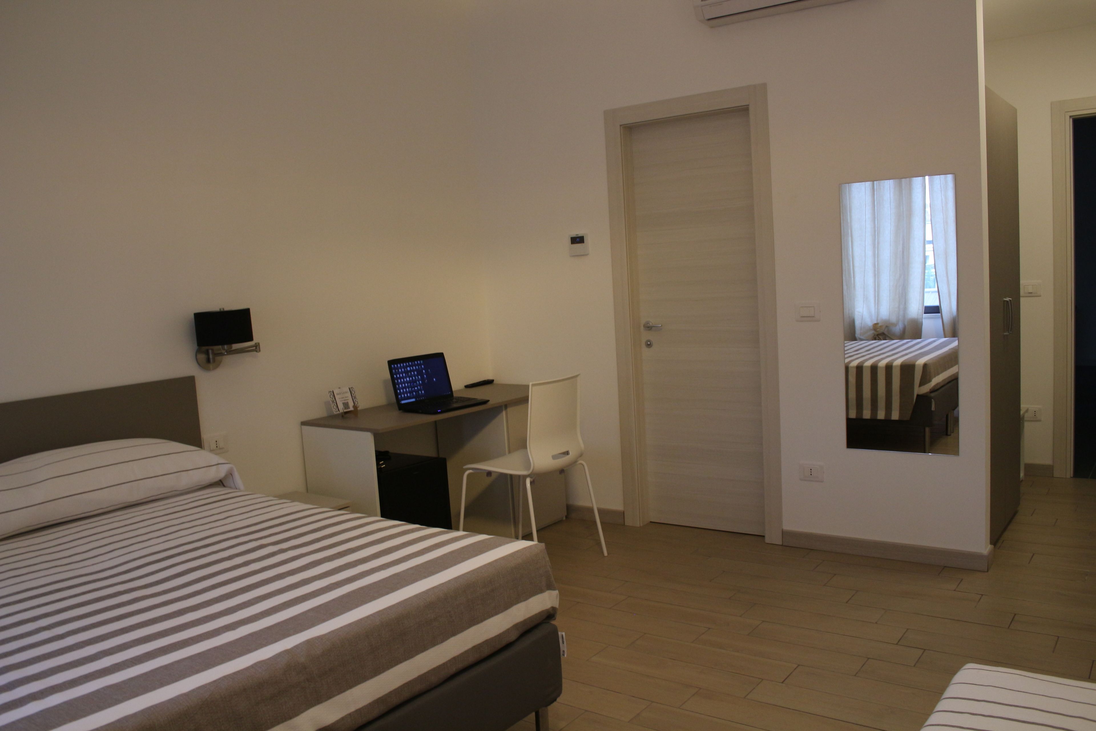 Quarto com cama, escrivaninha com laptop, cadeira e porta que dá para outro cômodo.