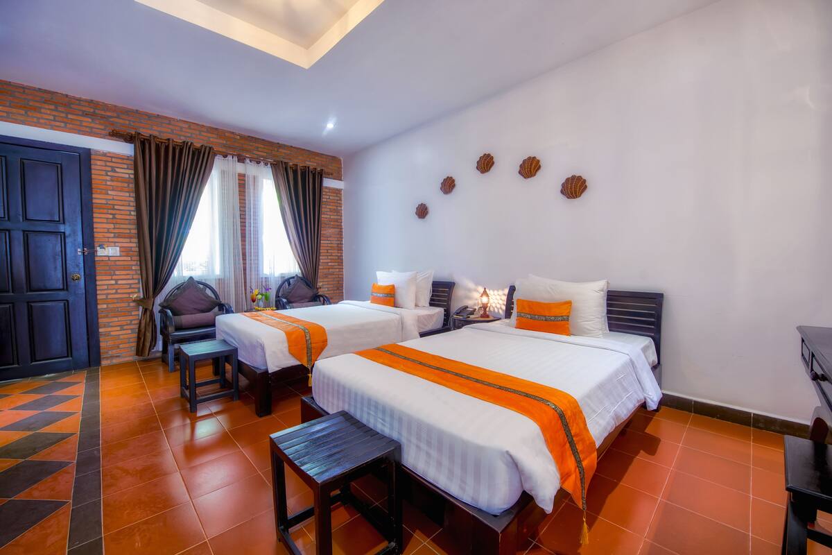 Quarto de hotel com duas camas, uma escrivaninha e uma cadeira.