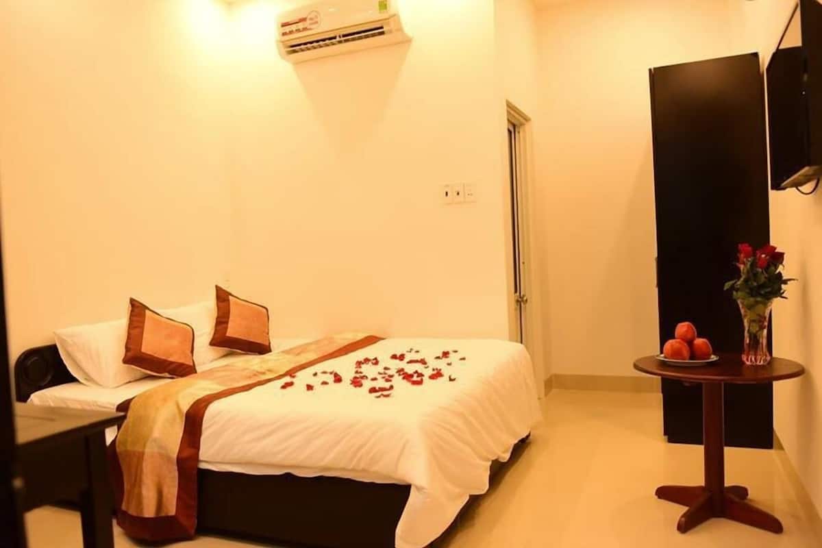 Quarto de hotel com cama, mesa de cabeceira com um vaso de flores e ar condicionado fixado na parede.