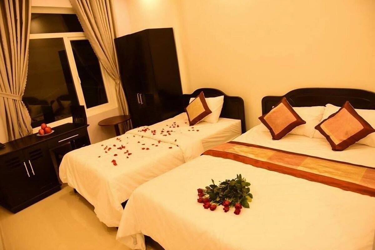 Quarto de hotel com duas camas, televisão, secretária e janela com cortinas.