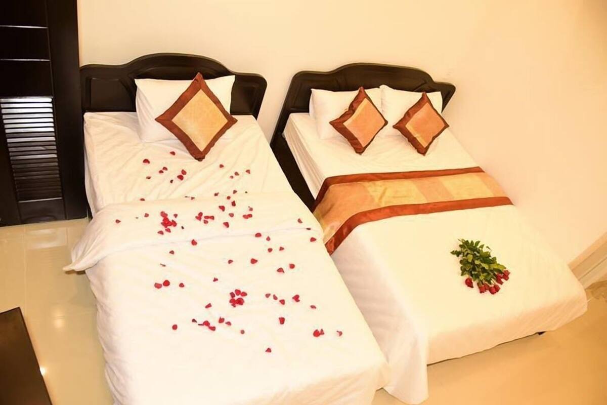 Duas camas com lençóis brancos, uma com pétalas de rosa e a outra com um buquê de rosas vermelhas.