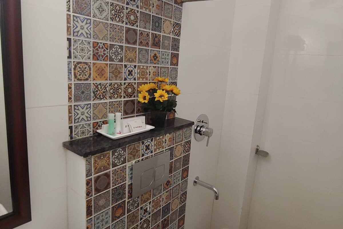 Casa de banho com revestimento de azulejos, suporte de toalhas, sanita e chuveiro.