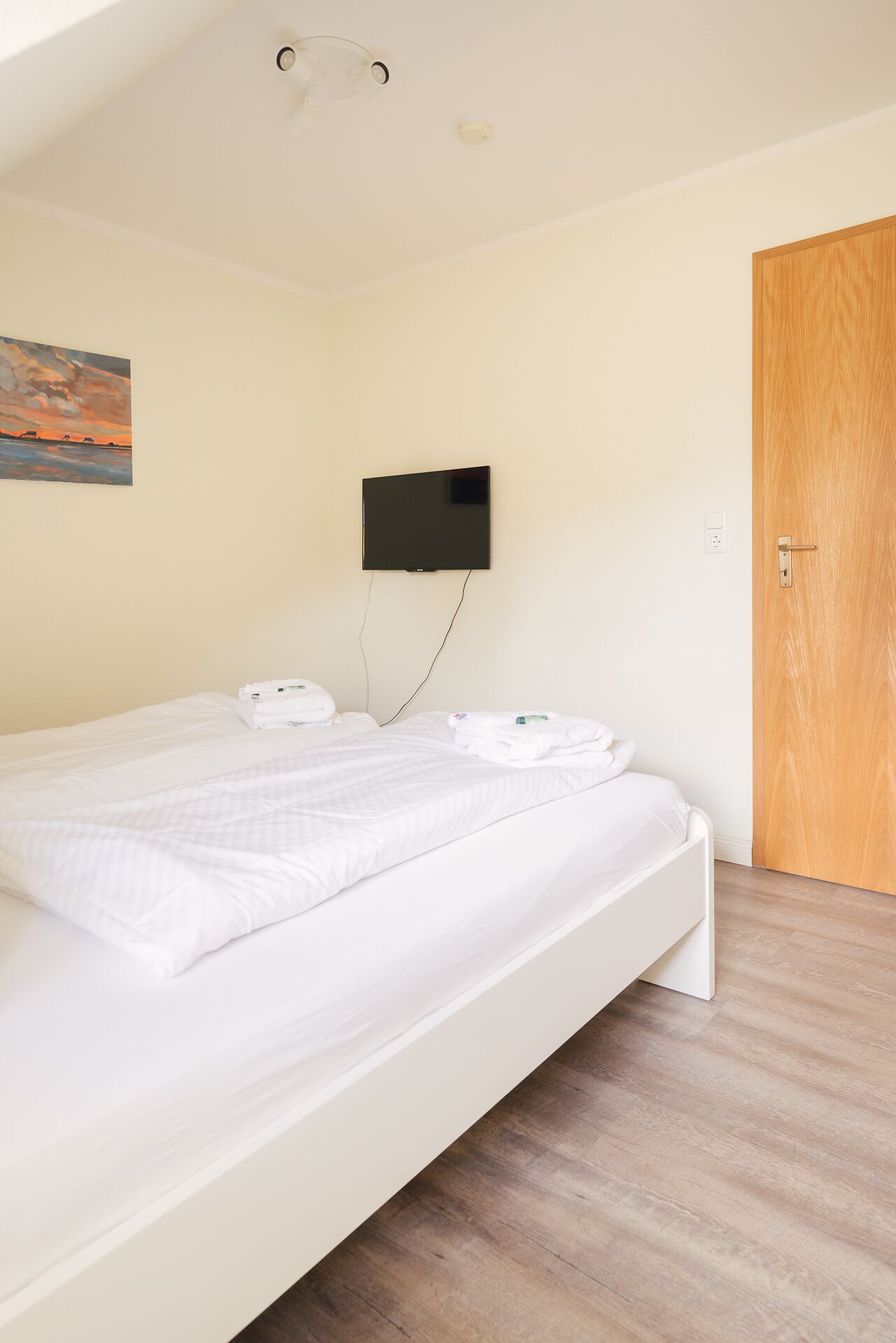 Quarto de hotel moderno com uma cama grande, uma televisão de tela plana na parede e uma porta de madeira.