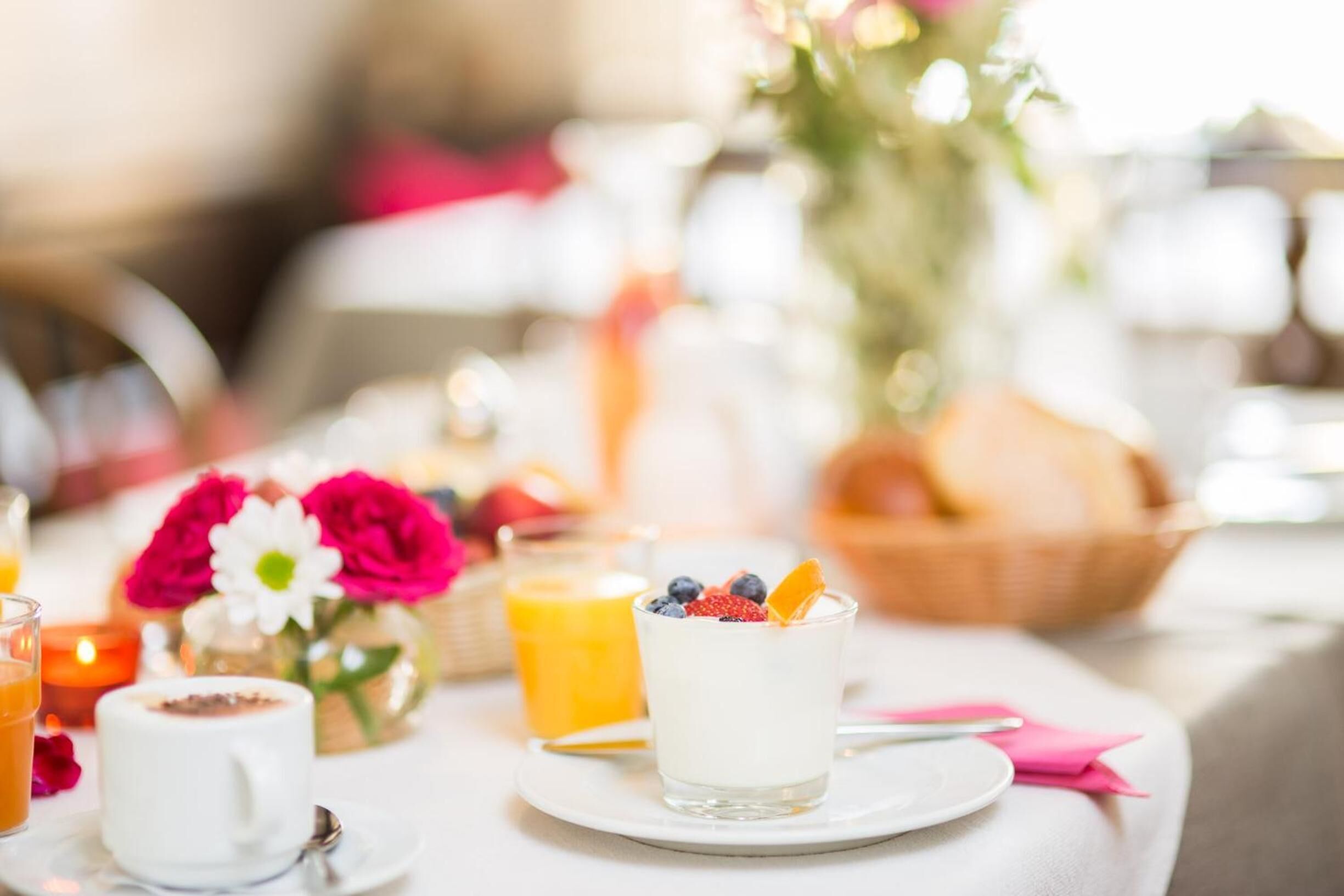 Um cenário de café da manhã com um copo de iogurte coberto com frutas vermelhas, uma fatia de laranja, uma xícara de café e um copo de suco de laranja.