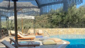 Área da piscina com espreguiçadeiras, parede de pedra e um grande guarda-sol.