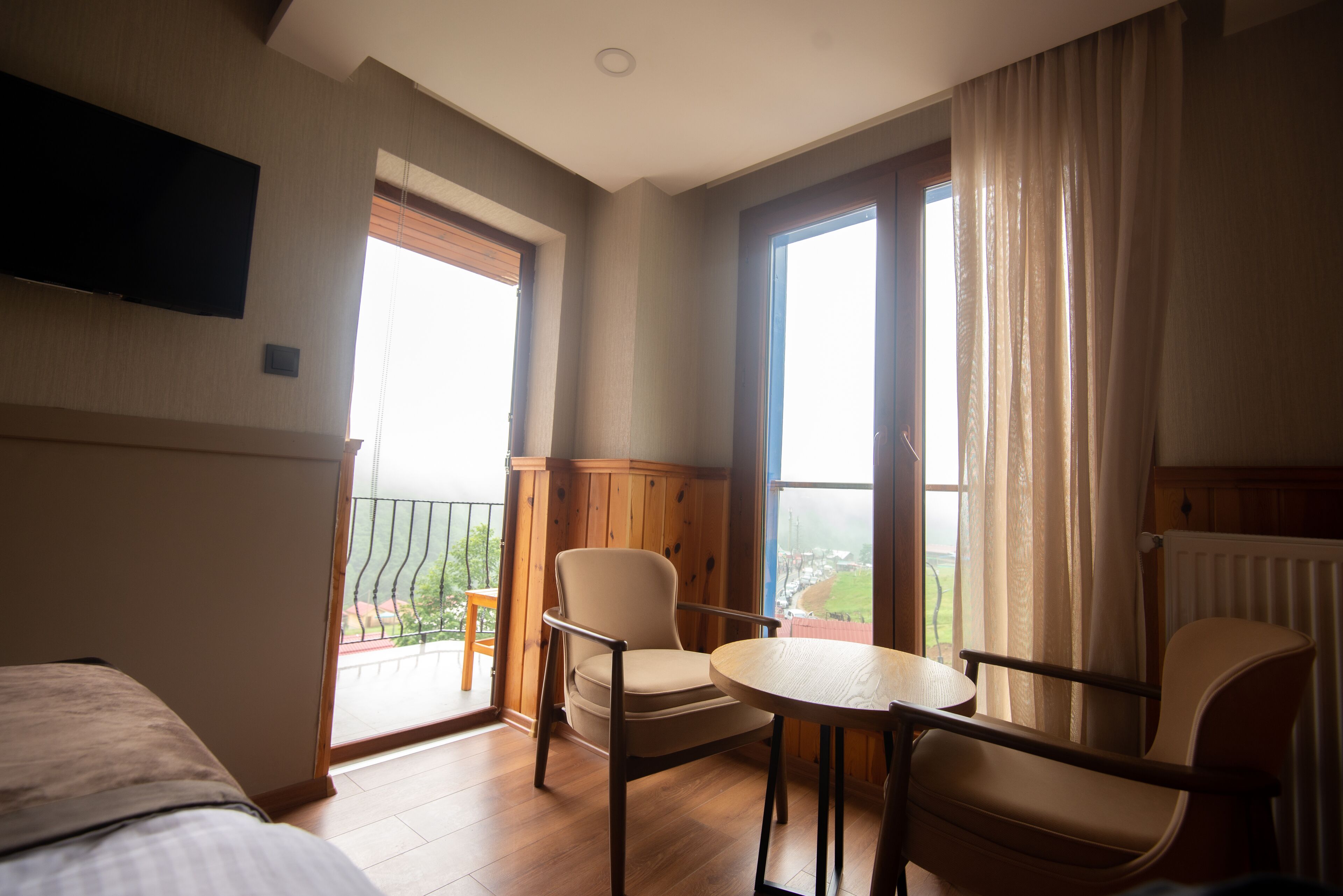 Quarto de hotel com cama, mesa pequena, duas cadeiras, televisão e varanda com vista.