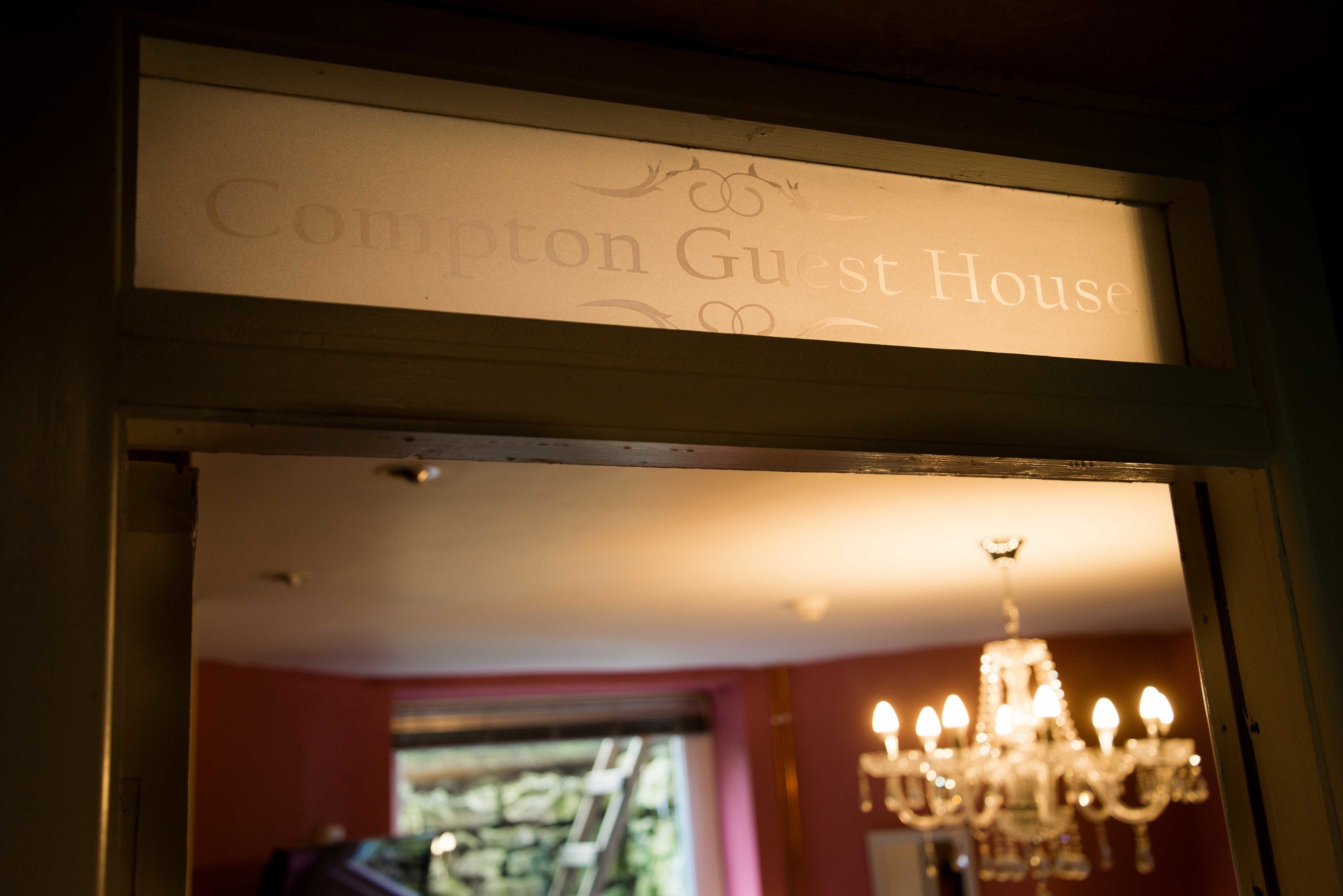 Uma placa com a inscrição 'Compton Guest House', com um candelabro visível ao fundo.