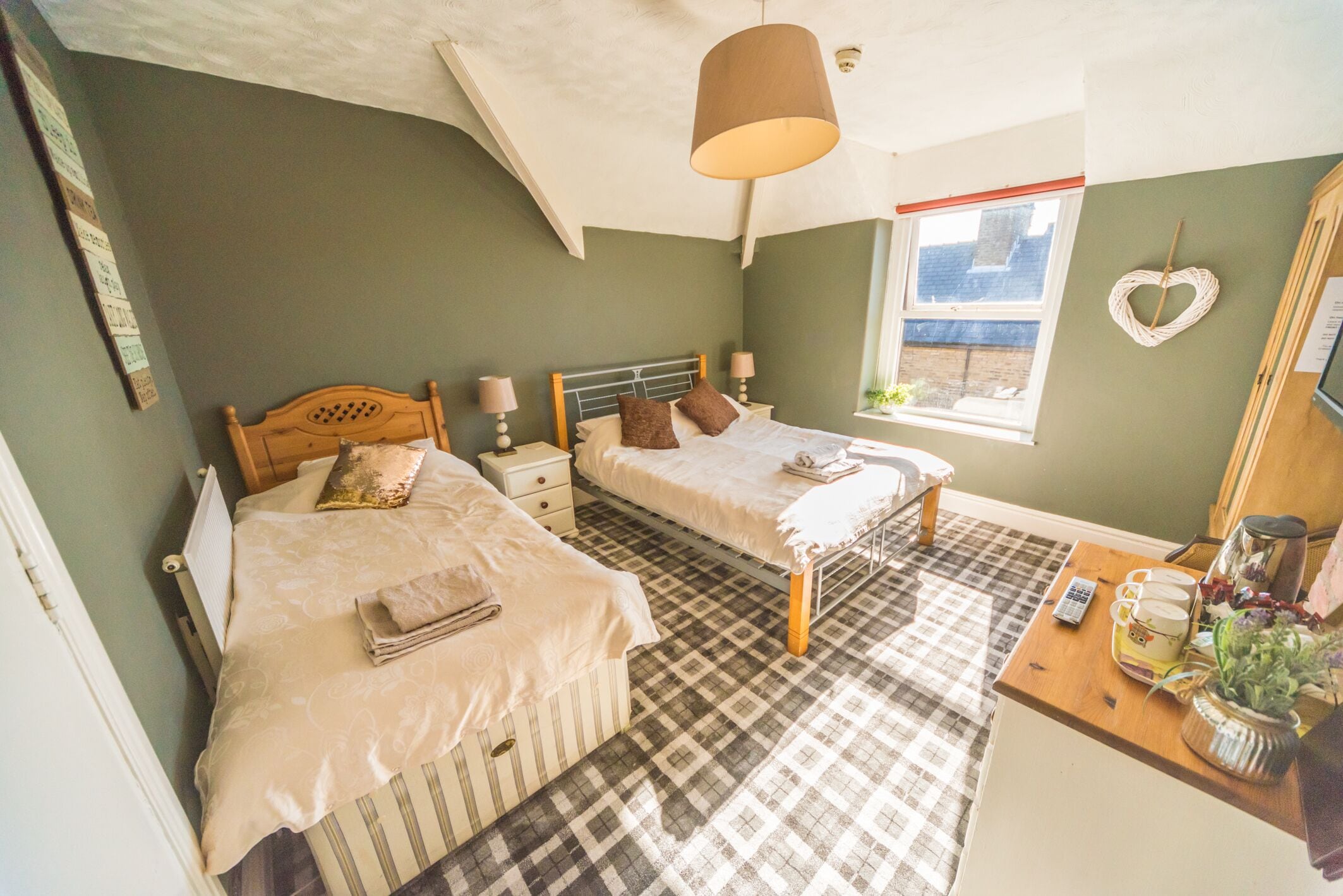 Quarto com duas camas, piso xadrez, janela com vista e mesa de cabeceira com luminária e planta.
