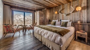 Quarto com decoração em madeira, uma cama grande, uma mesinha e uma cadeira.