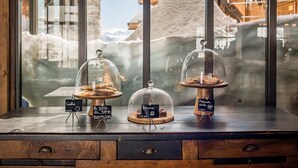 Exposição de sobremesas com três itens cobertos numa vitrine de loja, com vista para um monte nevado ao fundo.
