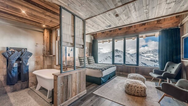 Quarto moderno com uma janela ampla, teto de madeira e vista para montanhas.