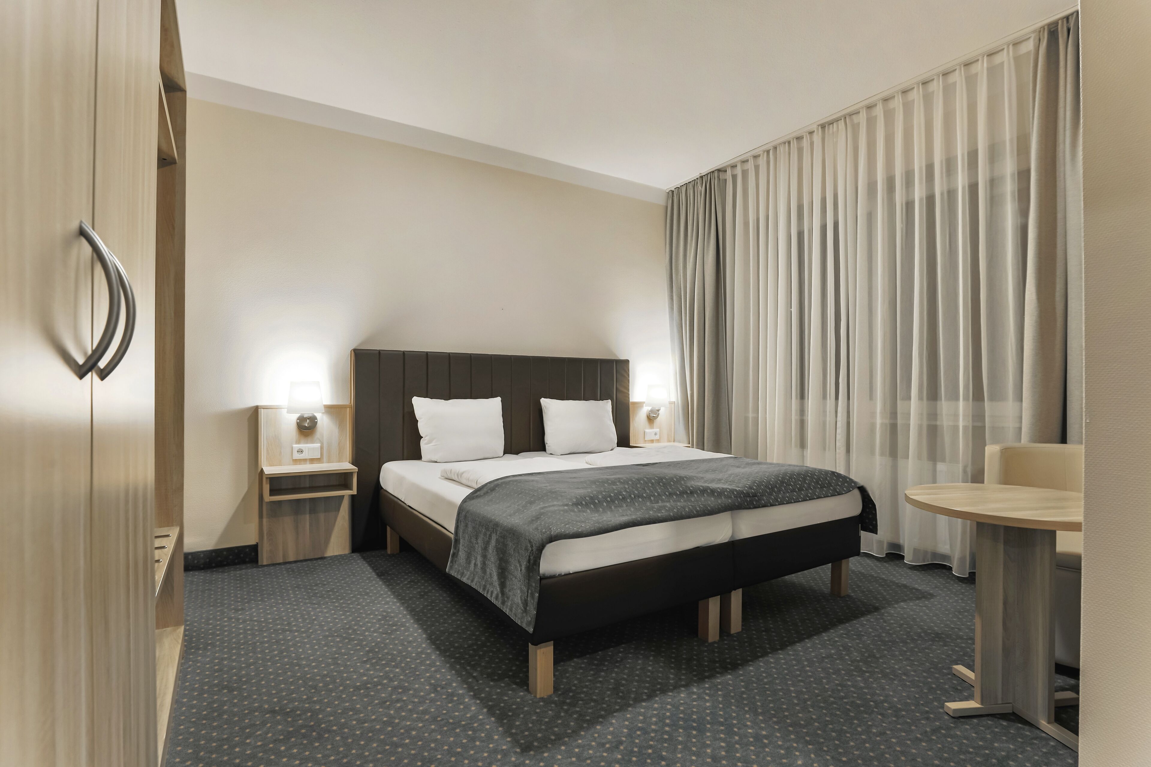 Quarto de hotel com cama, mesas de cabeceira, escrivaninha e uma cadeira.