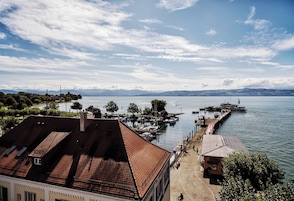Vista para o mar com um cais, barcos e uma cadeia montanhosa ao longe.