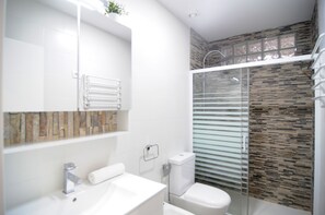 Uma casa de banho moderna com chuveiro em cabine de vidro, lavatório branco e sanita.