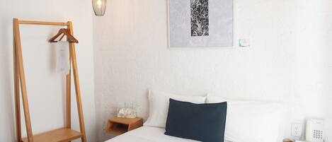Quarto de hotel bem arrumado com cama, um cabide de madeira, mesa de cabeceira com telefone e luminária fixada na parede.