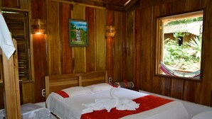Quarto de madeira com duas camas, um quadro na parede e janela com vista para o verde.