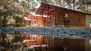 Uma cabana de madeira refletida em águas calmas, rodeada por árvores.