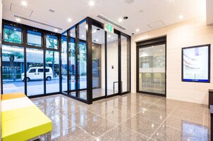 Um hall moderno com entrada de vidro, área de estar amarela e um painel digital na parede.