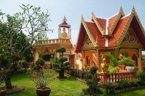 Um templo tailandês tradicional com uma estátua dourada, arquitetura elaborada e um jardim bem cuidado.