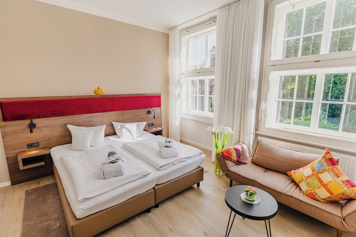 Quarto de hotel com cama, sofá, uma mesa pequena e janela com cortinas.