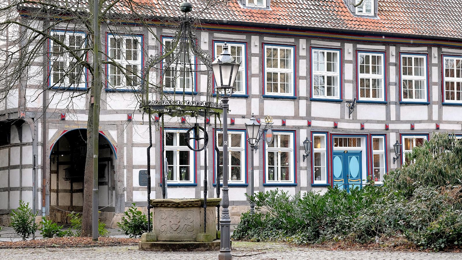 Um edifício europeu tradicional com fachada simétrica, várias janelas com detalhes azuis e uma entrada destacada com arco.