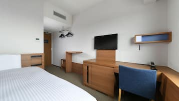 Quarto de hotel com uma cama grande, uma escrivaninha de madeira, uma cadeira, uma televisão e uma pequena mesa.