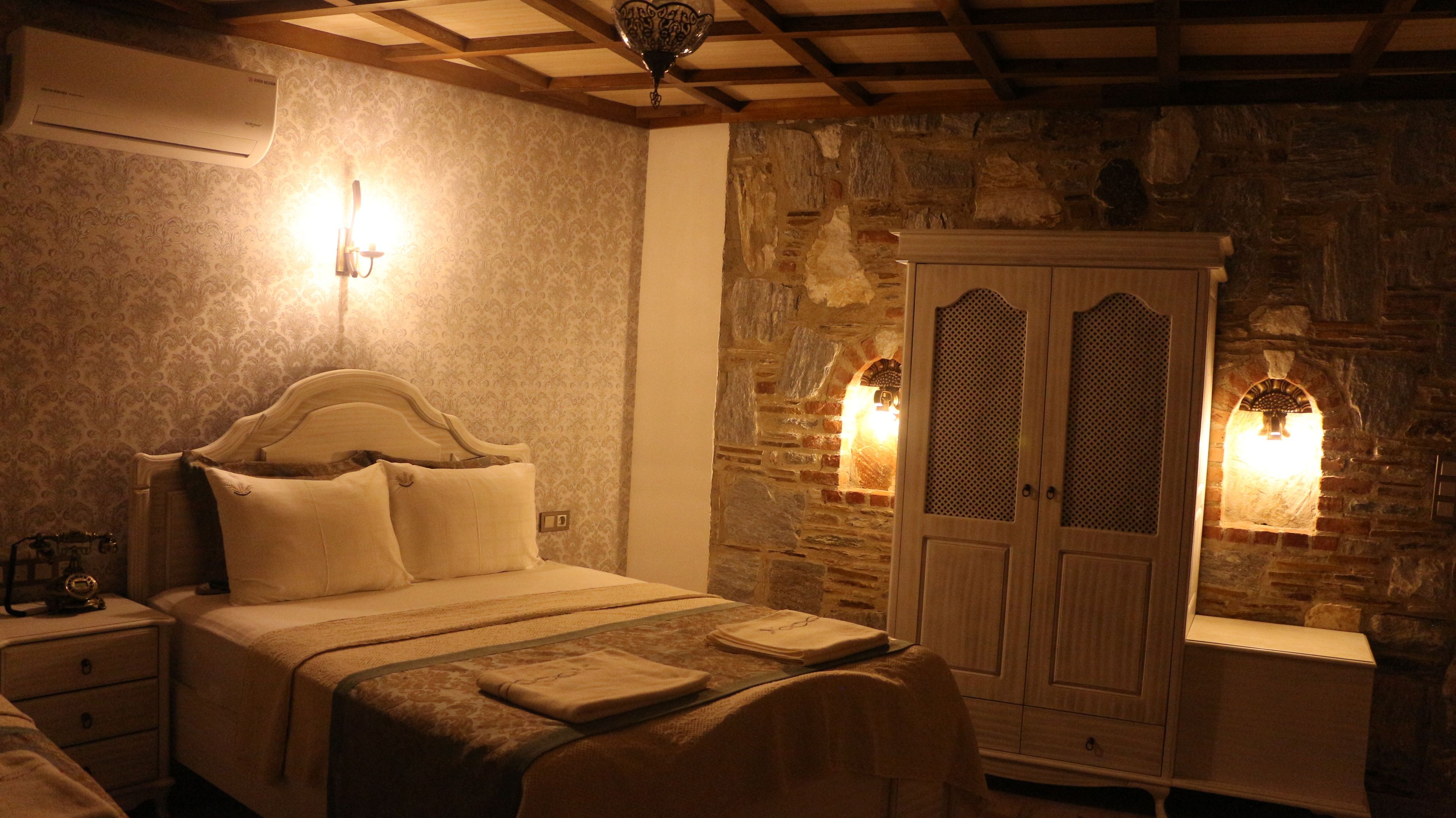 Quarto com cama, mesas de cabeceira, guarda-roupa e parede de pedra.
