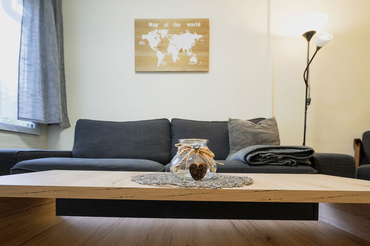 Uma sala de estar moderna com uma mesa de centro de madeira, um pote de vidro com decoração de coração e um mapa-múndi na parede.