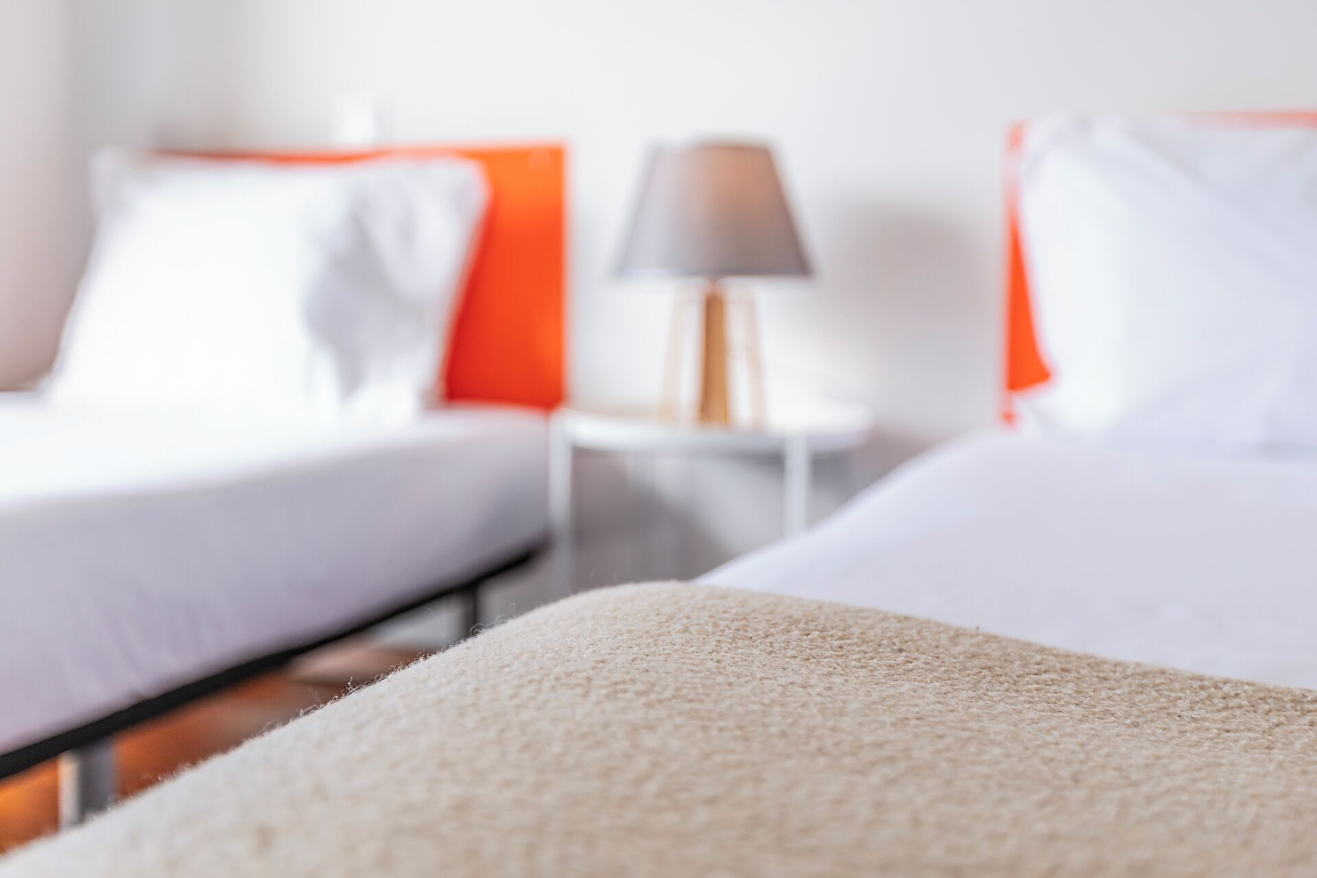 Quarto de hotel com duas camas, uma mesa de cabeceira e uma luminária.