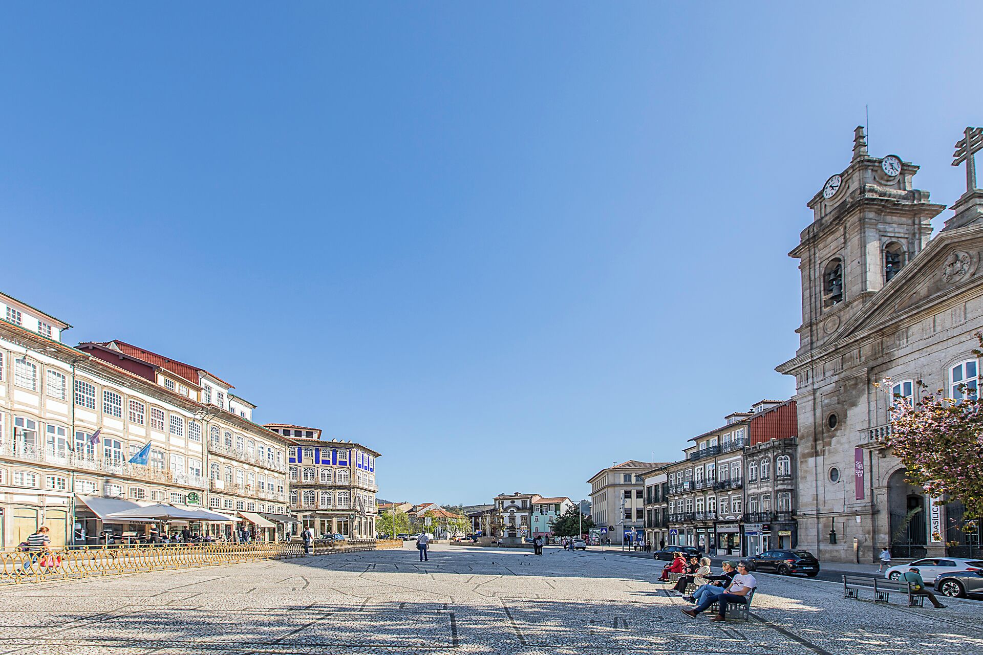 Uma praça histórica com calçamento de pedras, arquitetura clássica e uma torre do relógio imponente.