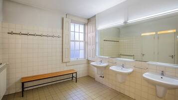 Uma casa de banho com duas pias, um banco, um espelho grande e uma janela.