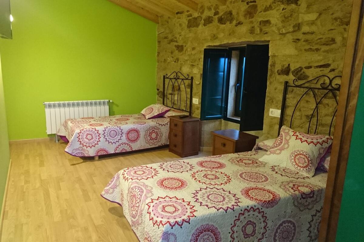 Quarto com duas camas, um radiador, piso de madeira e parede de pedra.