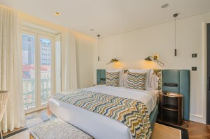 Quarto de hotel com uma cama grande, mesa de cabeceira, luminária e vista para o exterior.
