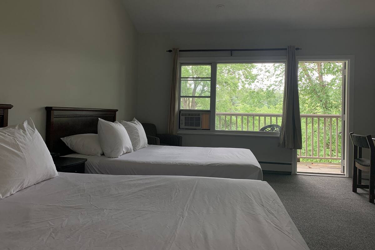 Quarto de hotel com duas camas, janela com vista para vegetação e varanda.