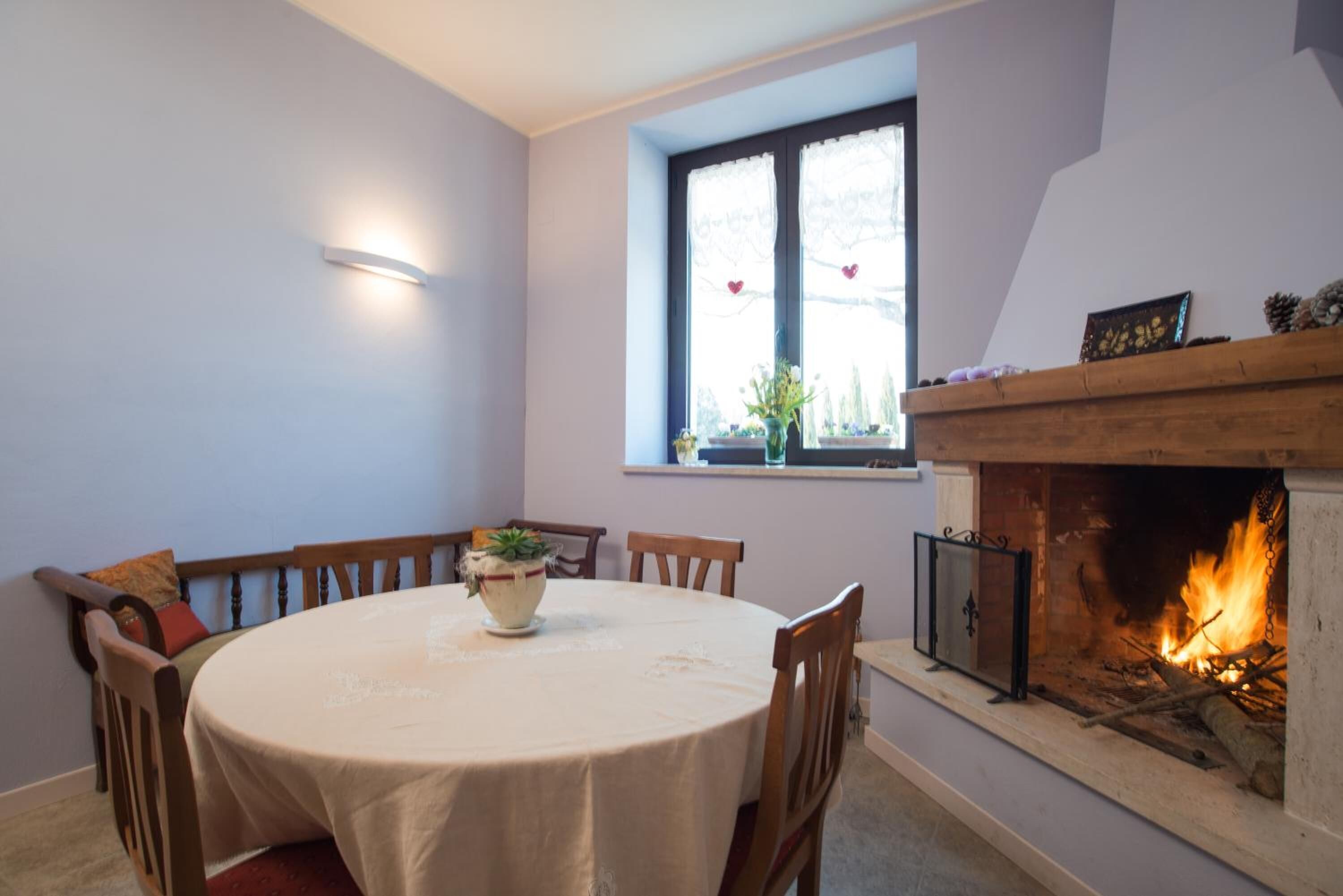 Uma sala de jantar com uma mesa redonda, cadeiras, lareira e uma janela com detalhes decorativos.