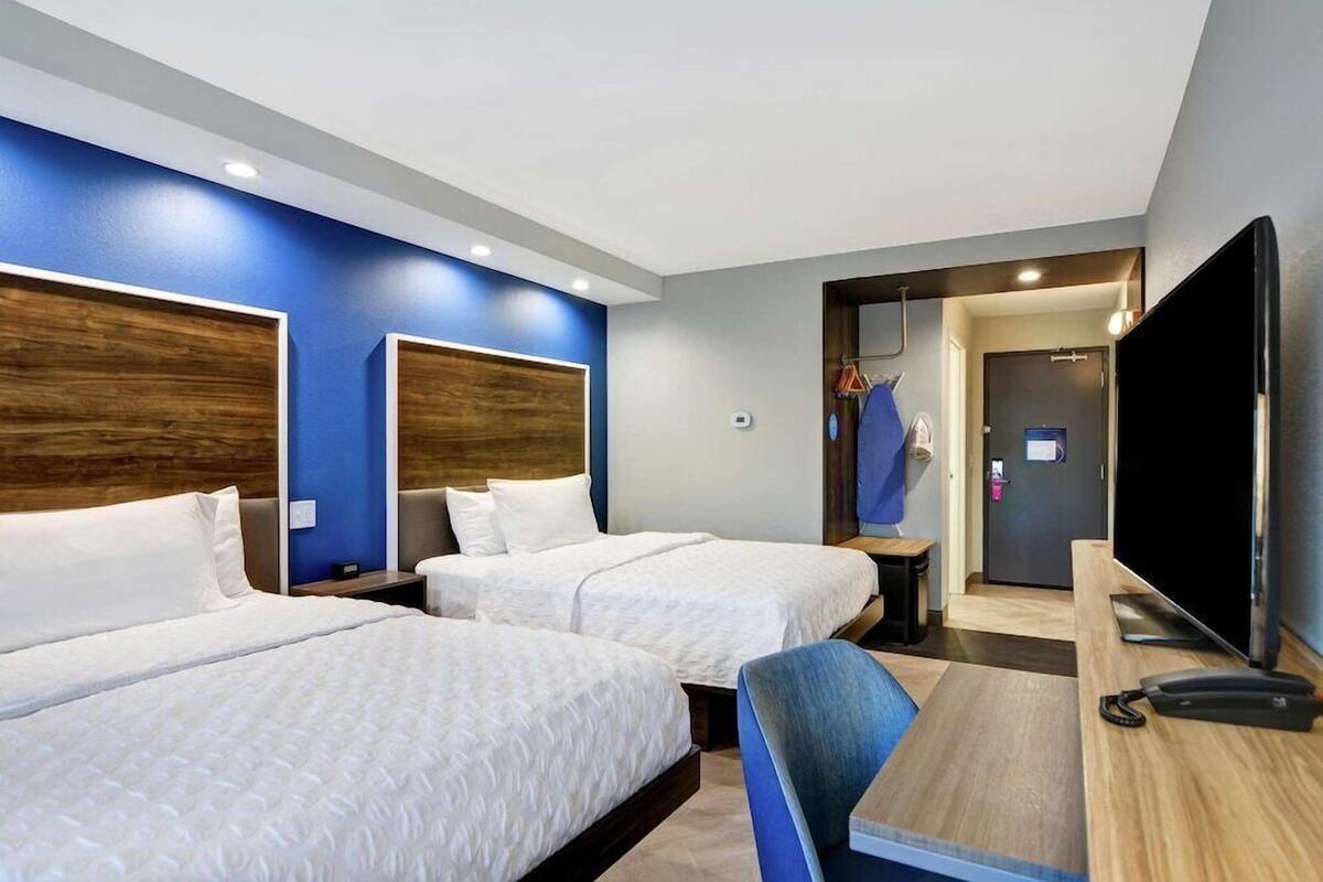 Quarto de hotel com duas camas, uma mesa com cadeira, televisão e porta para o banheiro.