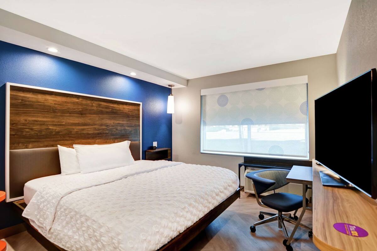 Quarto de hotel com uma cama grande, uma mesa, uma cadeira, uma televisão e janela com vista.