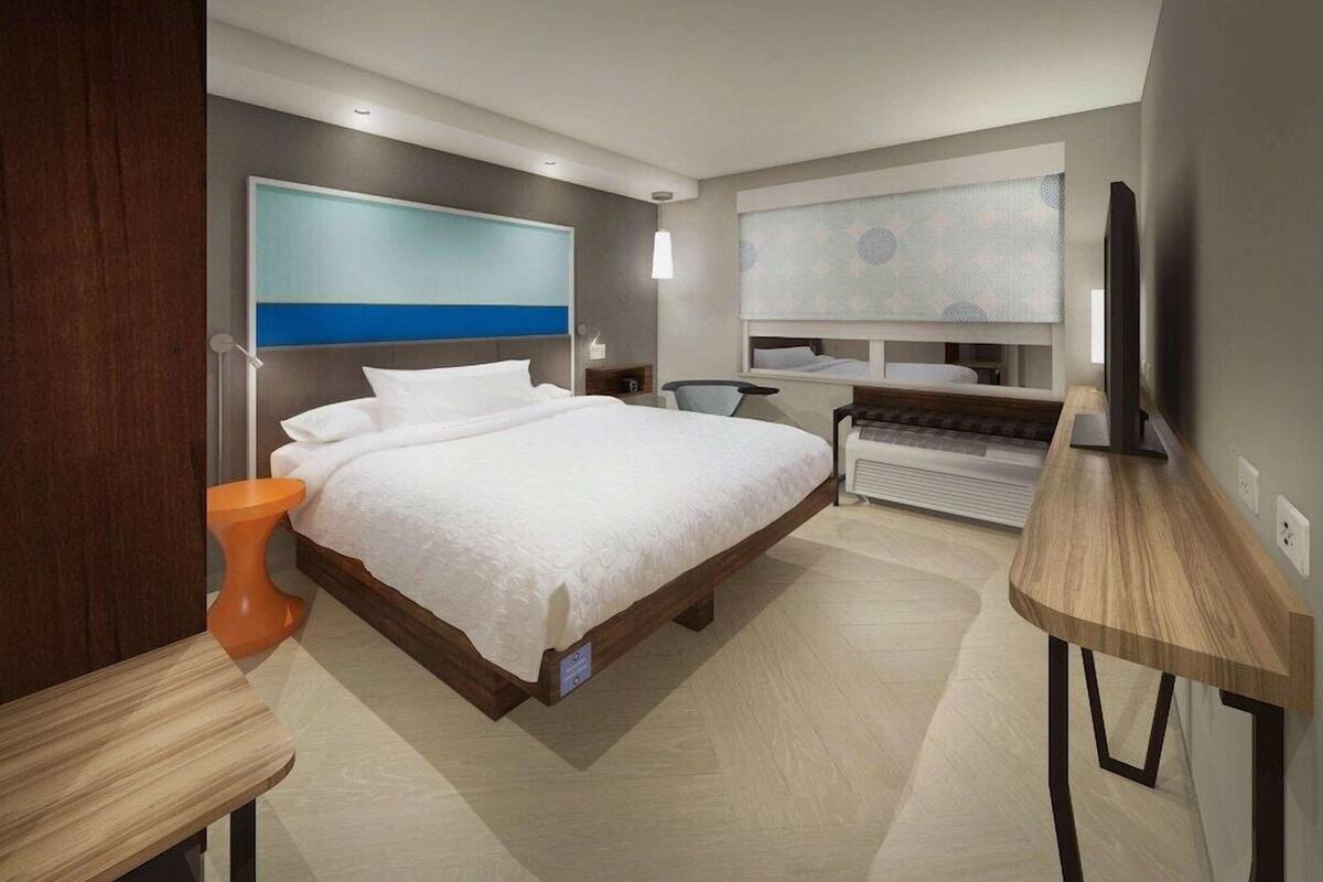 Quarto de hotel moderno com uma cama grande, uma escrivaninha, uma cadeira, uma televisão e uma janela com vista.