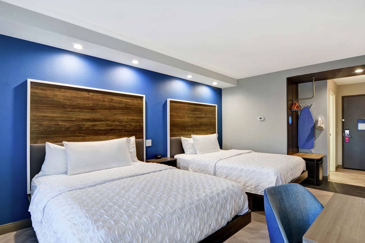 Quarto de hotel com duas camas, cabeceira de madeira, escrivaninha e uma cadeira.