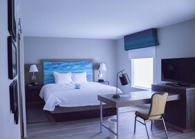 Quarto de hotel com cama, escrivaninha, cadeira, televisão e janela.
