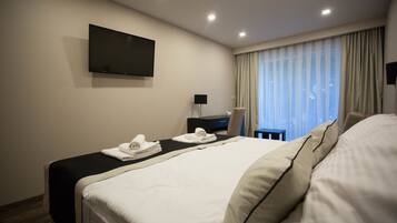 Quarto de hotel com cama, televisão de tela plana na parede, escrivaninha com luminária e janela com cortinas.