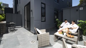 Um pátio moderno ao ar livre com uma mesa de jantar, cadeiras de vime e um buffet com comida e bebidas.