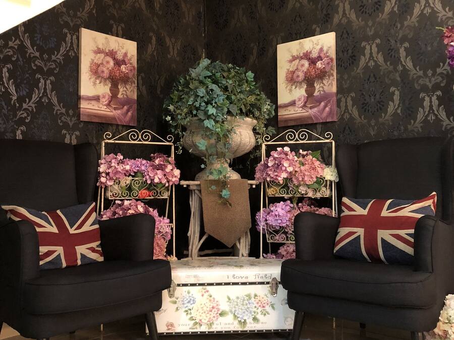 Um quarto com duas poltronas pretas, uma mesa decorativa com um arranjo floral e duas imagens emolduradas na parede.