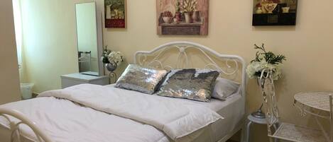 Quarto bem arrumado com cama, mesa de cabeceira, espelho e quadros nas paredes.