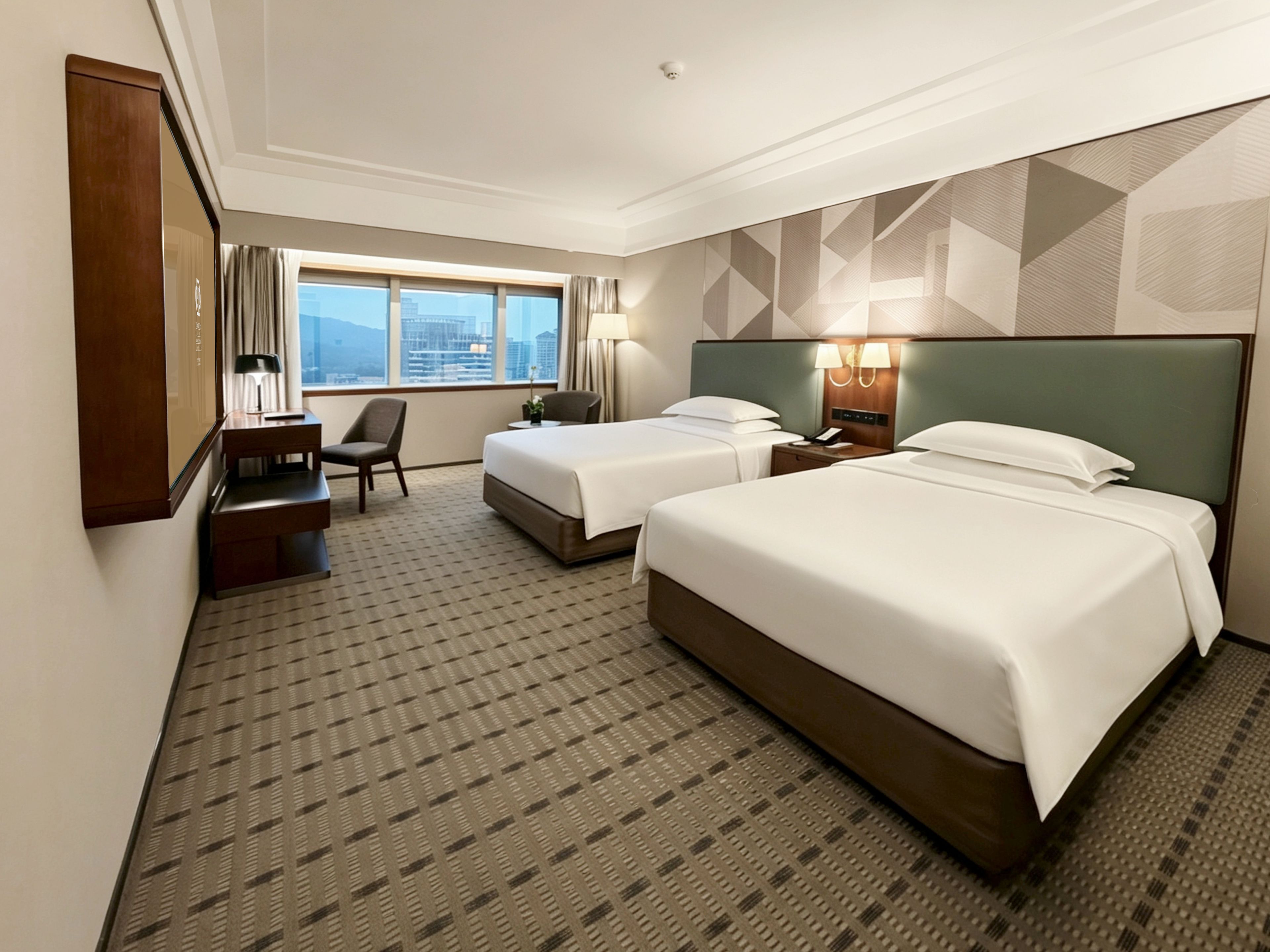 Quarto de hotel com duas camas, uma escrivaninha, uma cadeira, janela com vista para a cidade e carpete estampado.