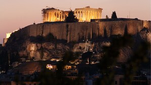 O Parthenon numa colina, rodeado por edifícios.