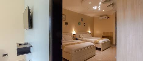 Quarto de hotel com duas camas, uma televisão fixada na parede, uma mesa de cabeceira e um candeeiro de teto.