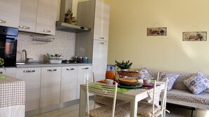 Cozinha moderna com área de jantar, incluindo fogão, pia e armários. Há uma mesa com cadeiras e um sofá na sala de estar.
