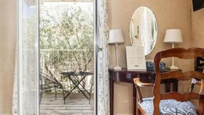 Quarto com cadeira de madeira, mesa pequena, espelho e vista para uma varanda externa com mesa e cadeiras.